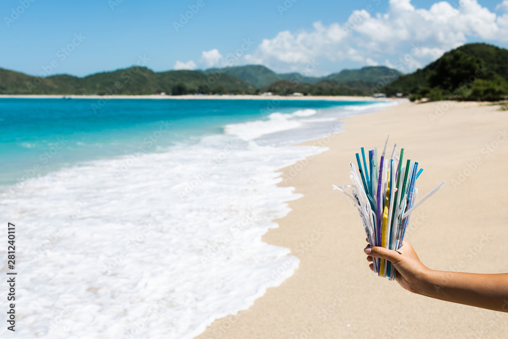 Hand holding heap of used plastic straws on background of clean beach ...