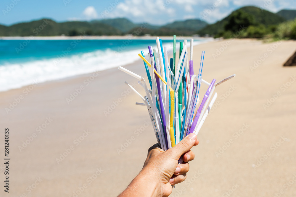 Hand holding heap of used plastic straws on background of clean beach ...