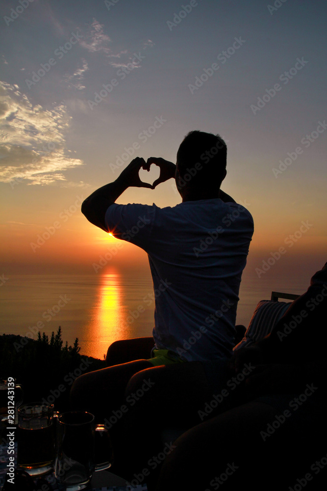 Boy enjoying sunset, watching and making heart shape sign on sun rays ...