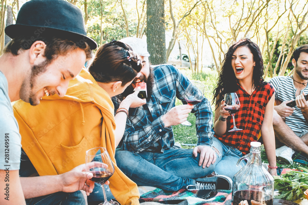 summer picnic party friends sitting on ground in park drinking red wine ...