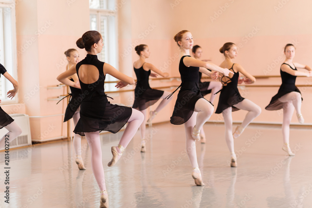 Medium group of teenage girls in black dresses practicing ballet moves ...