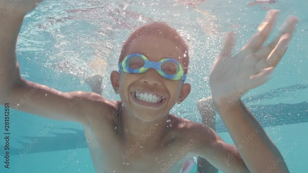 funny little boy swimming underwater in pool smiling waving hand ...