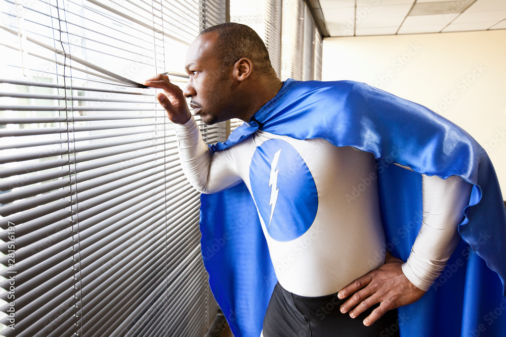Businessman in super hero costume looking through window Stock Photo ...