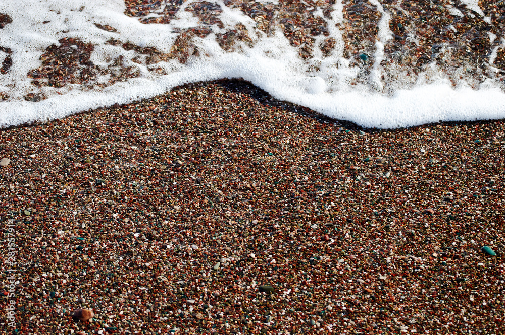 slow transparent sea wave with white foam cover the sand and pebbels on ...