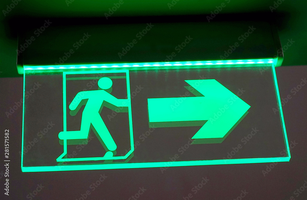 Illuminated fire or emergency exit sign,hung on wall,in a public place ...