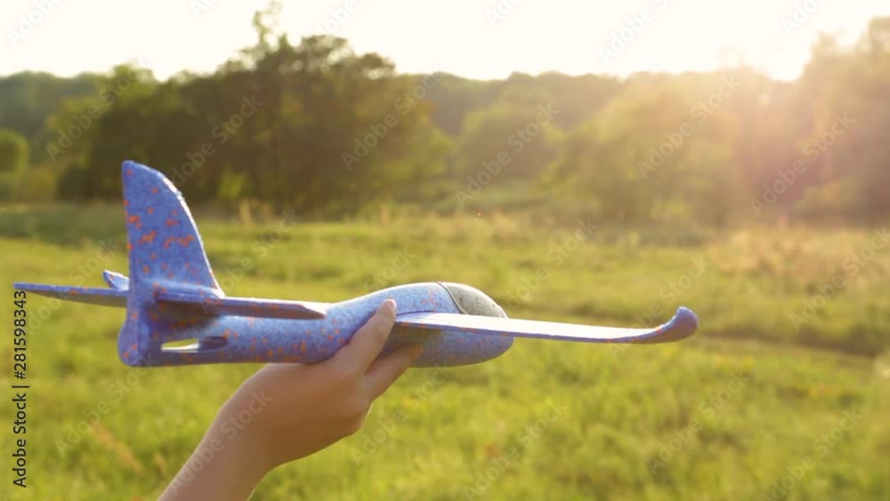 Young happy kid playing blue plastic toy plane outside on summer sunset ...