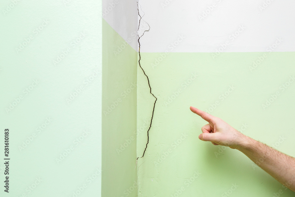 Man's hand finger pointing to cracked corner wall in house. Building ...