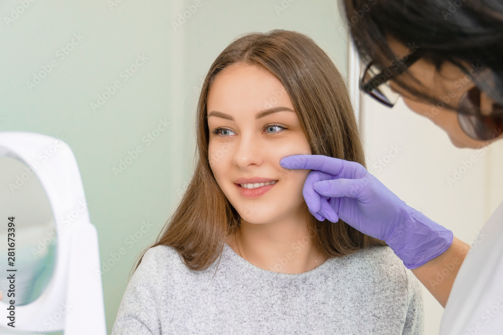 Female cosmetologist showing to young smiling woman the face zones to ...