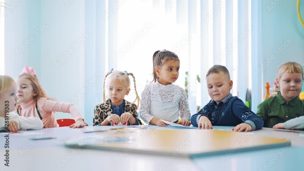Group of little students at a circle table during the lesson. Children ...