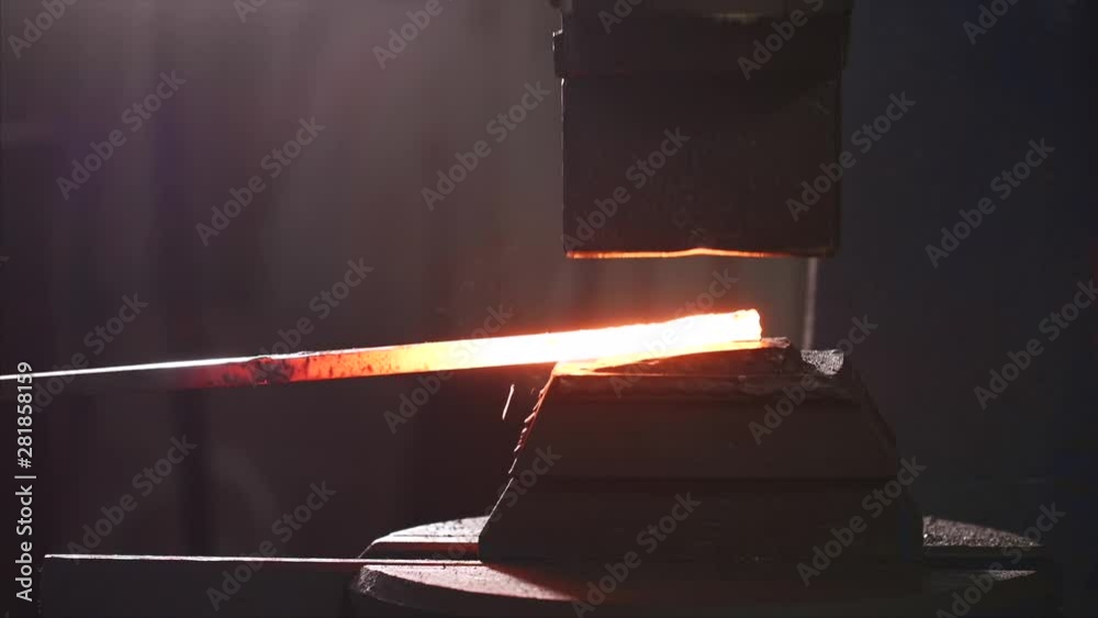 Using hammer machine for shaping hot red metal bar in forge workshop ...