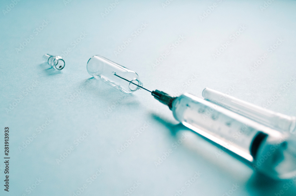 sterile syringe with a needle and an ampoule of medicine on a blue ...