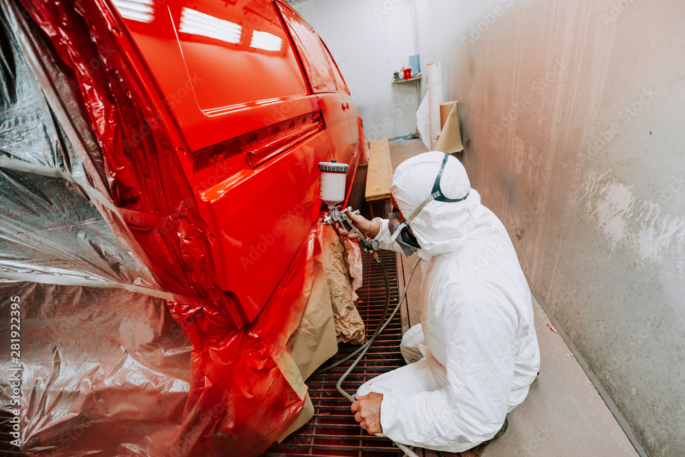 Portrait of Painter working and painting a red car in paint garage ...