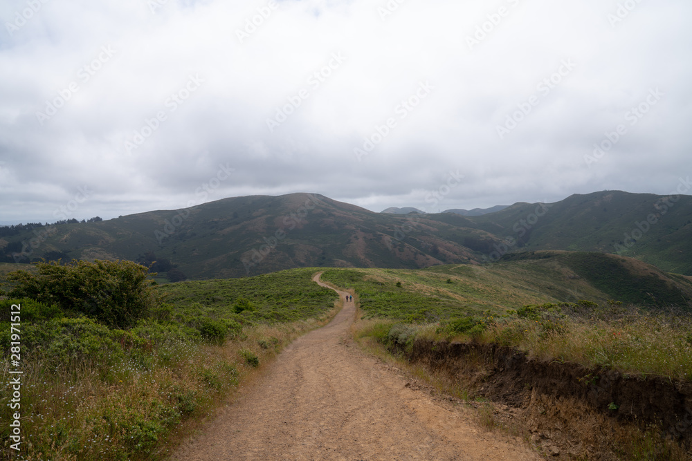 Long, winding hiking trail leading to mountains with two hikers ...