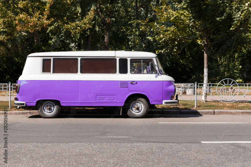 purple Retro van standing on the road near the fence, a park in the ...