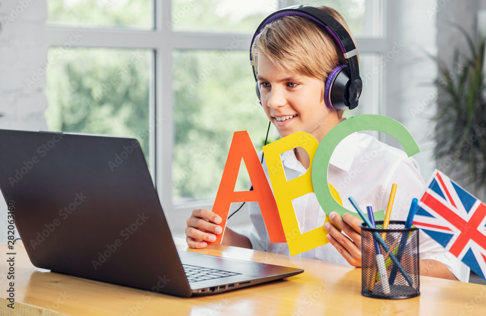 Young schoolboy learning english using online course with laptop ...