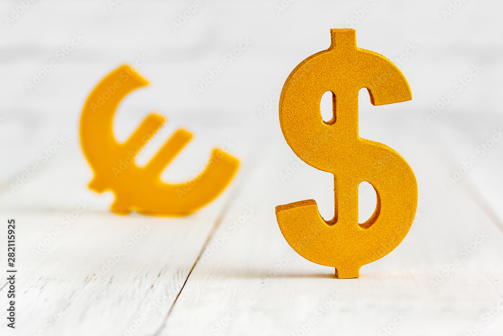 Dollar sign over euro sign on white wood table over white brick ...