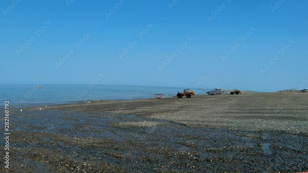 Two tractors on beach; in background a tractor is towing a fishing ...