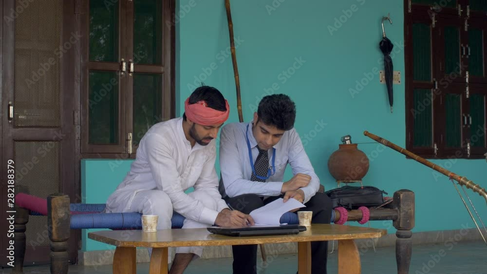 Young attractive bank agent guiding Indian farmer to fill-up new bank ...