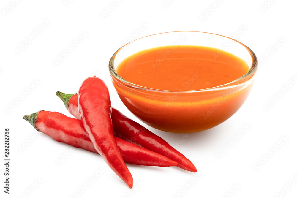 Peri peri chilli sauce in a glass bowl next to three red chillies ...