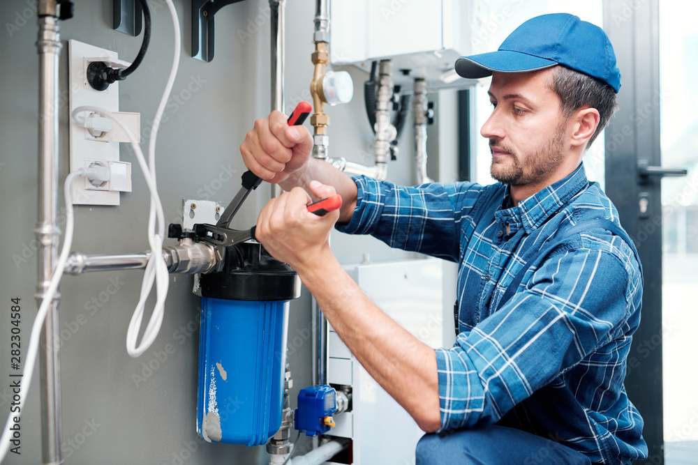 Young plumber or technician installing or repairing system of water ...