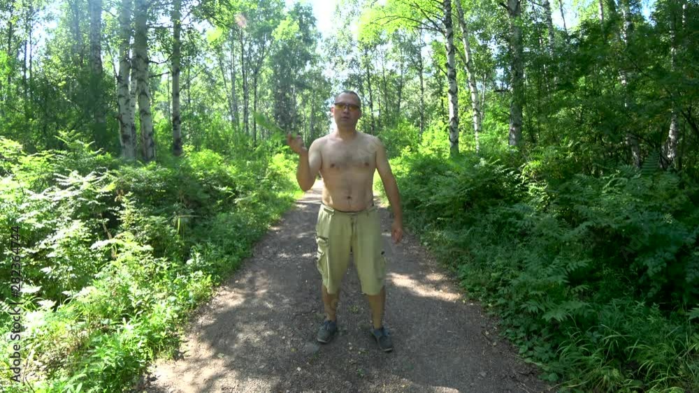 A man in a forest is fanning himself with a branch from mosquitoes ...