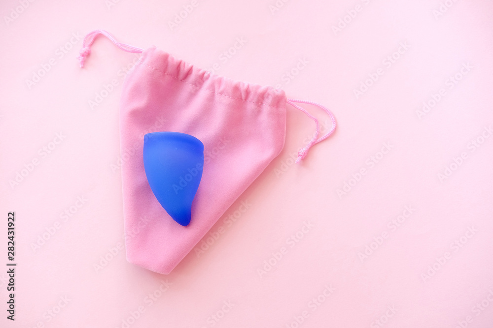 Blue menstrual cup and bag on pink background. Bag shaped as uterus ...