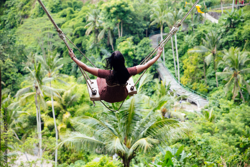 Young tourist woman swinging over the tropical rainforest at Bali ...
