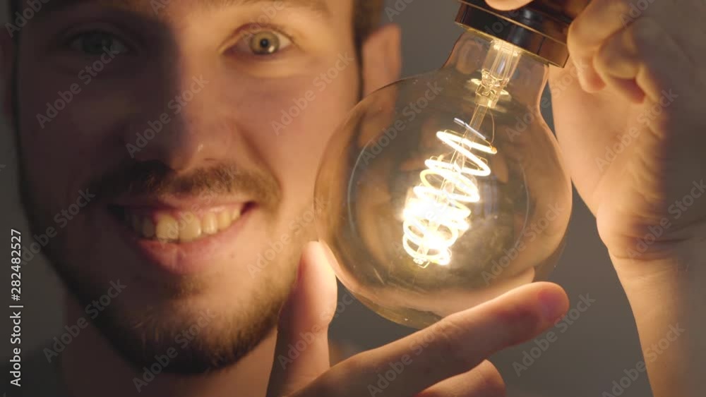 Close-up of smiling bearded man screw in and out a light bulb on the ...