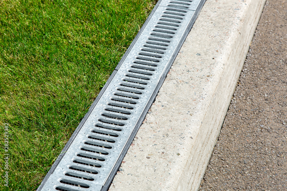 iron drainage system, closeup of an iron grille along a asphalt road ...