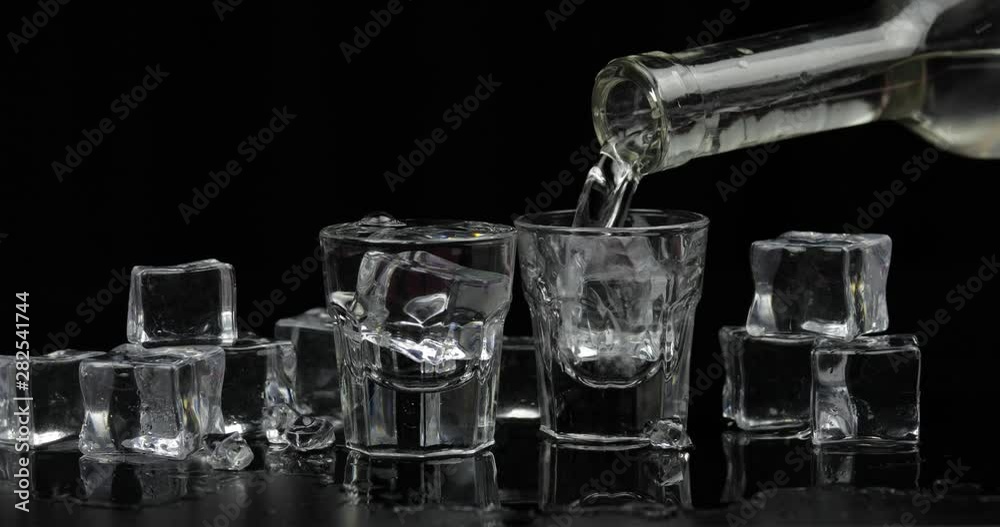 Pouring up two shots of vodka from a bottle into glass. Black ...