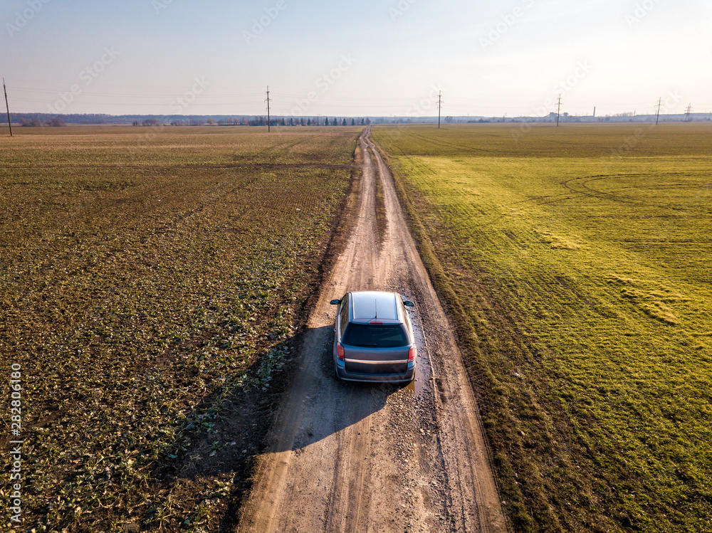 Aerial view of car driving by straight ground road through green fields ...