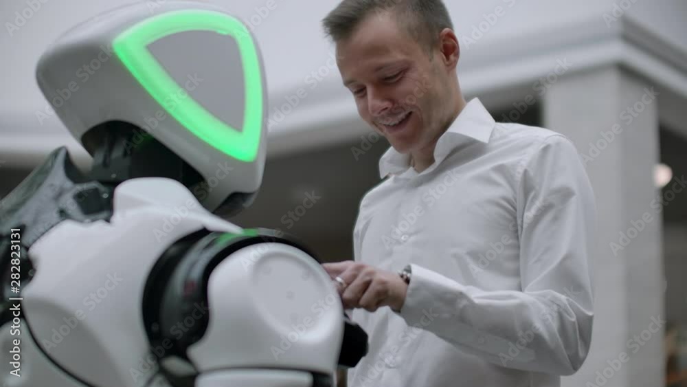 A man in a shirt communicates with a white robot asking questions and ...