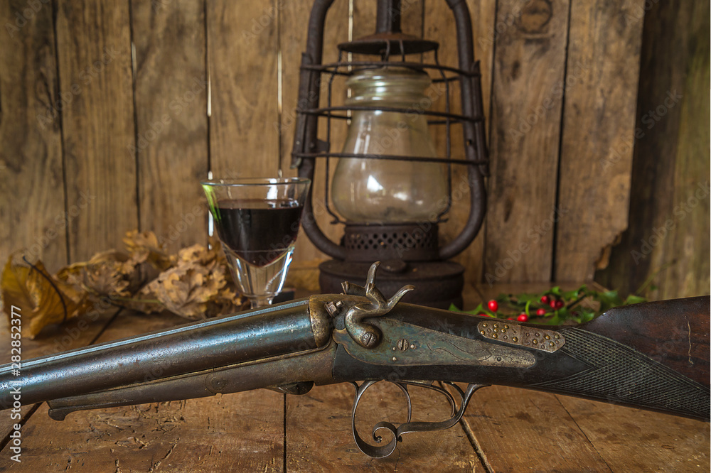 Still life with vintage hunting rifle, hurricane lamp and glass of red ...