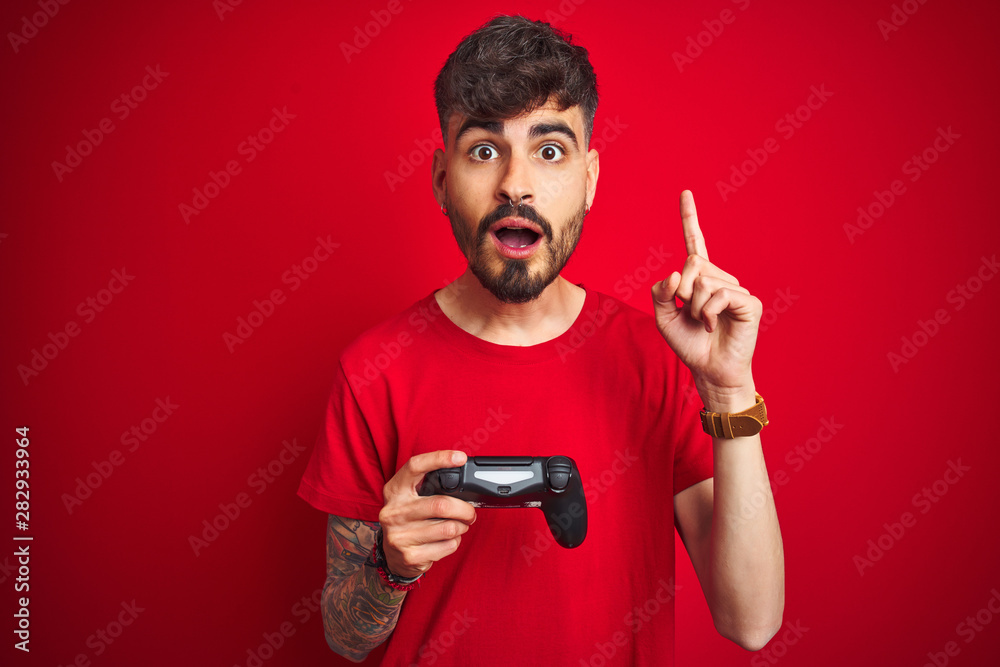 Young gamer man with tattoo playing video game standing over isolated ...