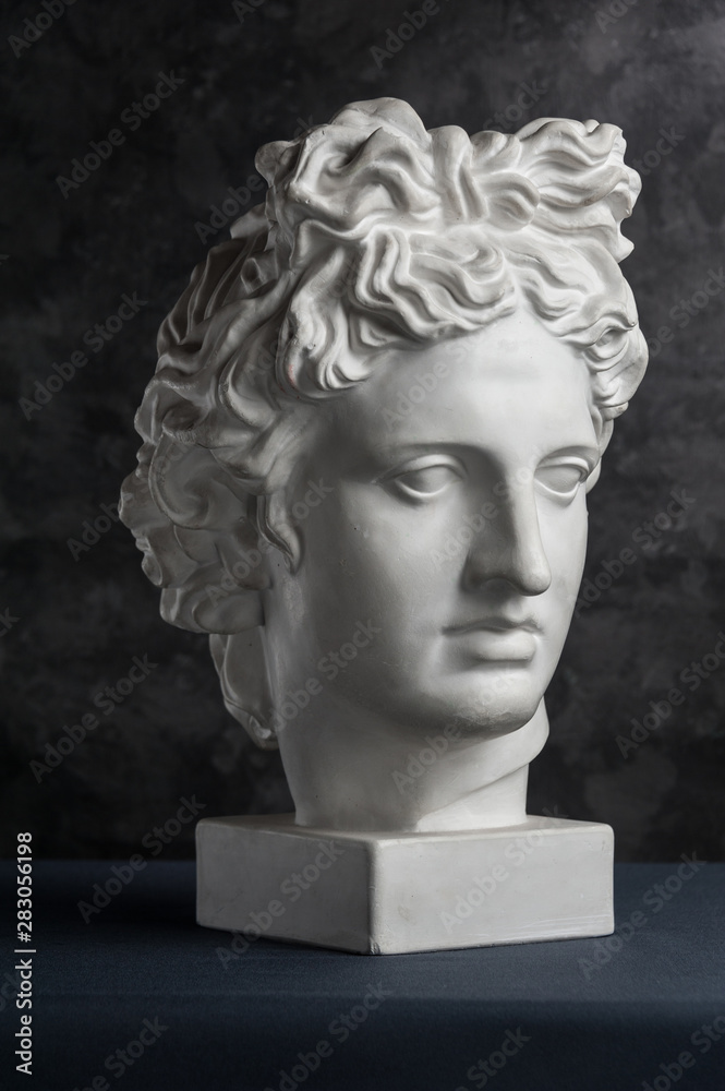Gypsum copy of ancient statue Apollo head on dark textured background ...