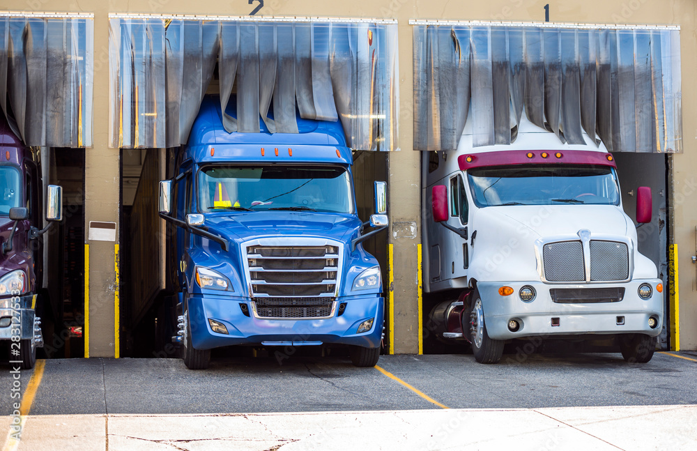 Row of big rigs semi trucks standing inside of warehouse loading ...