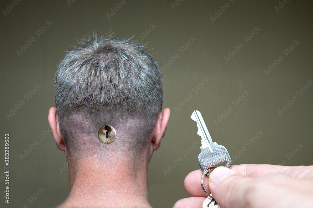 Hand with a key near a male head with a keyhole in the back of the head ...