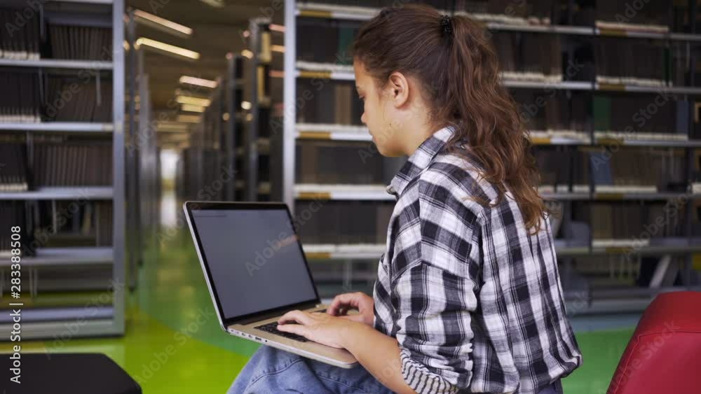 Pretty young girl with laptop in interior of modern library or high ...