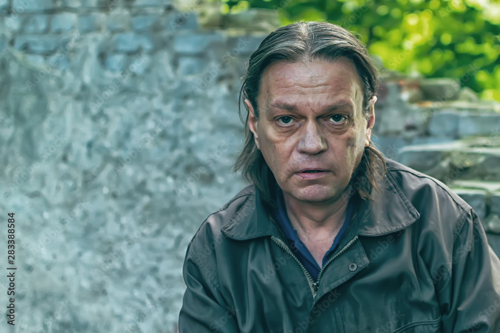a homeless man with a bruise on his cheek sitting in the ruins. Poverty ...