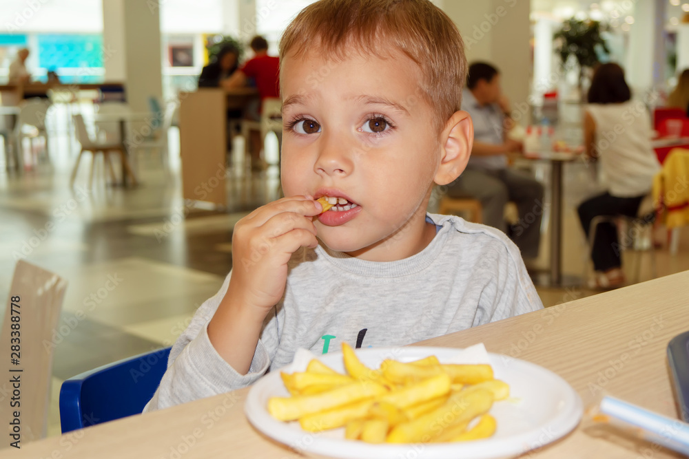 little child eating french fries sitting at a table on the food court ...