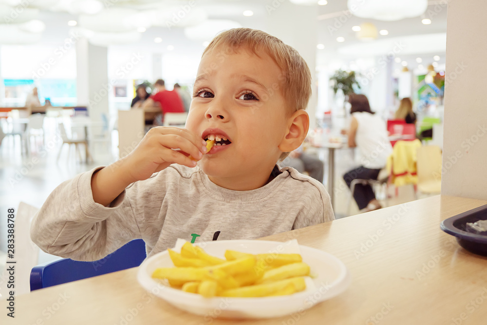 little child eating french fries sitting at a table on the food court ...