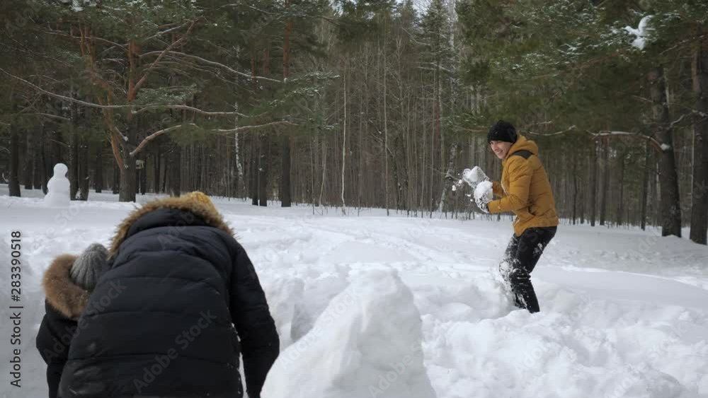 Man is playing snowballs with his family in winter park. His wife and ...