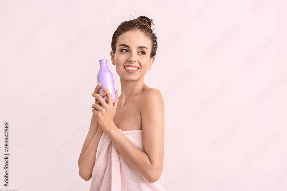 Beautiful young woman with bottle of shampoo against light color ...