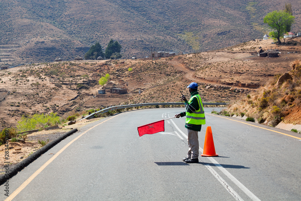 Road worker holds in hand red flag prohibiting traffic, travel ...