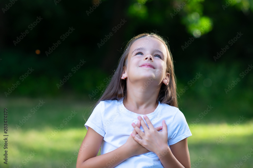 Little girl looking up to at sky with hands on chest, summer nature ...