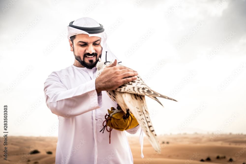 Arabic man with traditional emirates clothes walking in the desert with ...