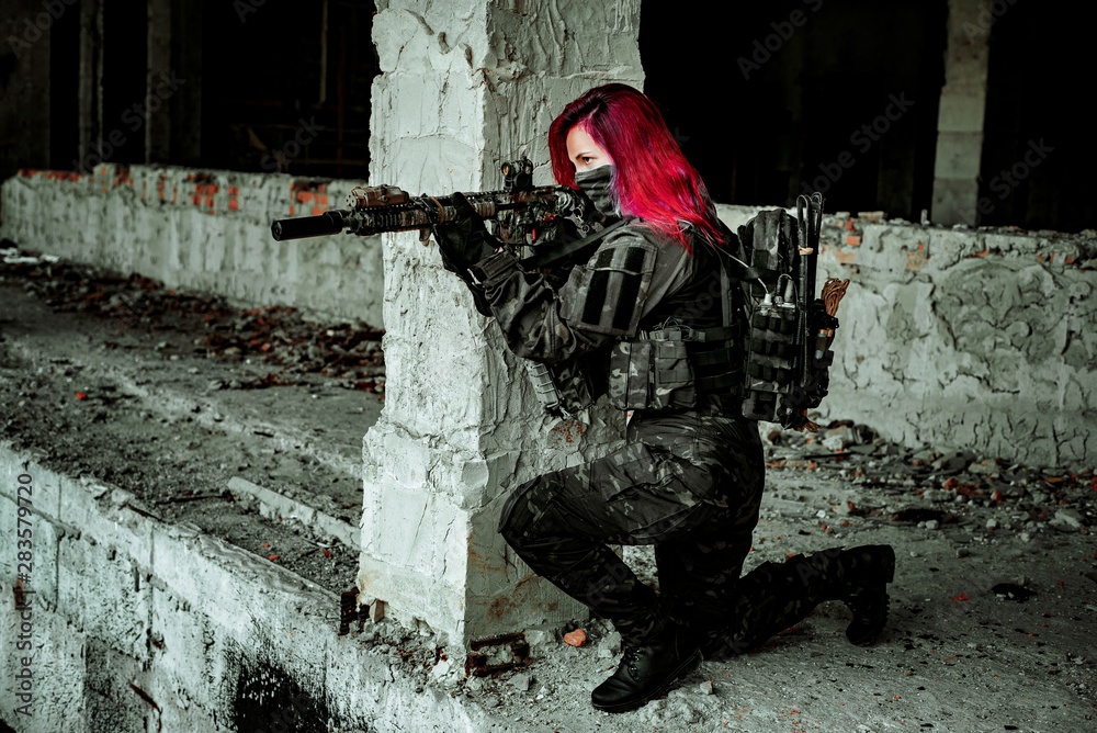 Red-hair airsoft woman in uniform with machine gun on one knee beside ...