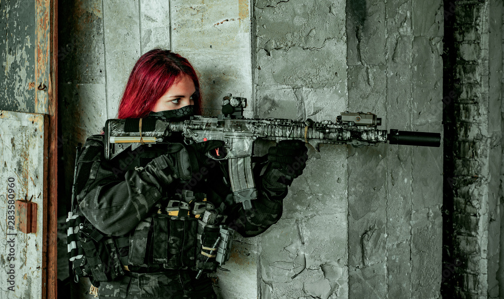 Airsoft red-hair woman in uniform with machine gun lurk beside concrete ...