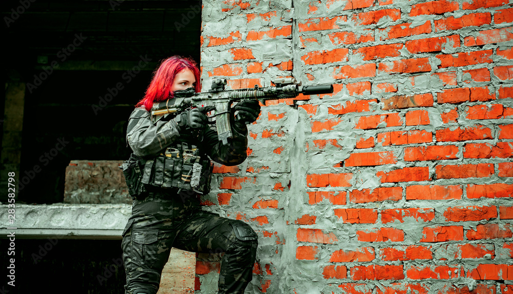 Airsoft red-hair woman in uniform with machine gun beside brick wall ...