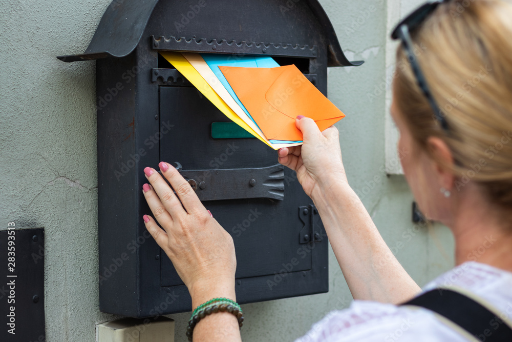 Mail carrier is inserting letters into mailbox. Woman is holding ...